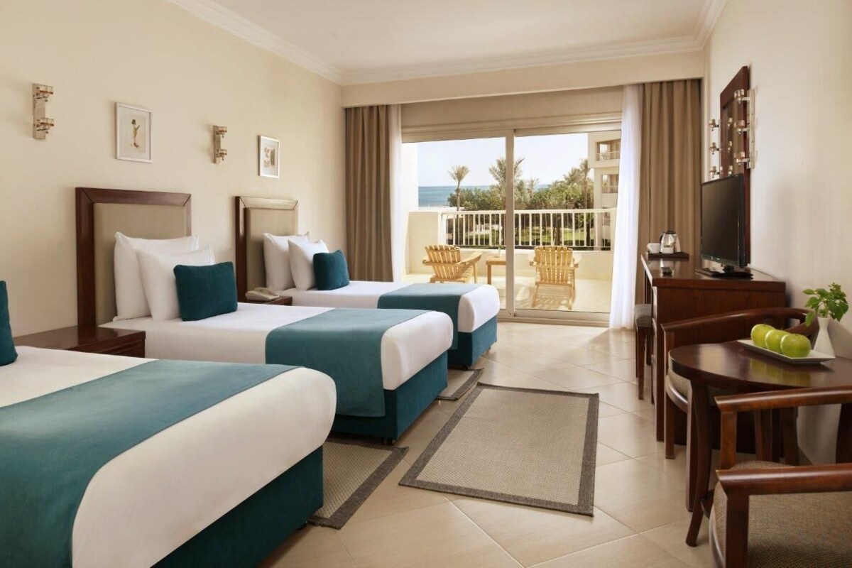 Quarto de hotel com duas camas, uma escrivaninha, uma televisão e uma varanda com vista.
