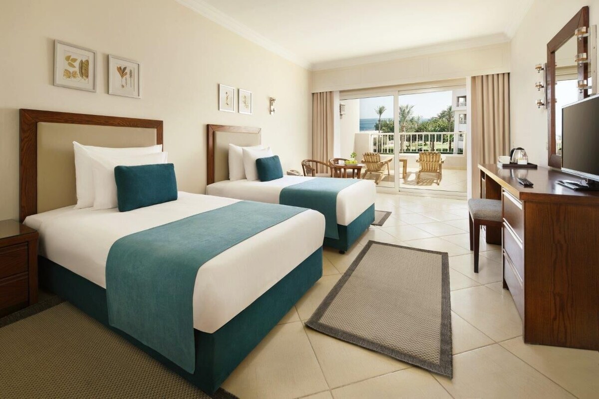 Quarto de hotel com duas camas, uma escrivaninha, televisão e varanda com vista.
