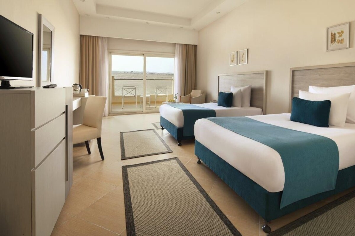 Quarto de hotel com duas camas, televisão, escrivaninha e varanda com vista.