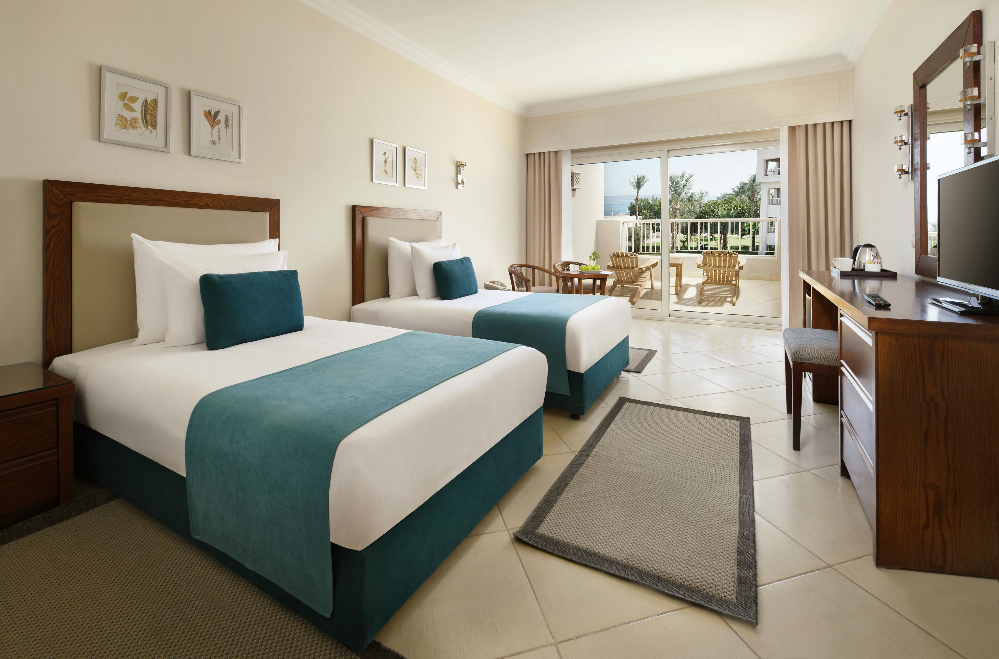 Quarto de hotel com duas camas, uma escrivaninha, televisão e varanda com vista.