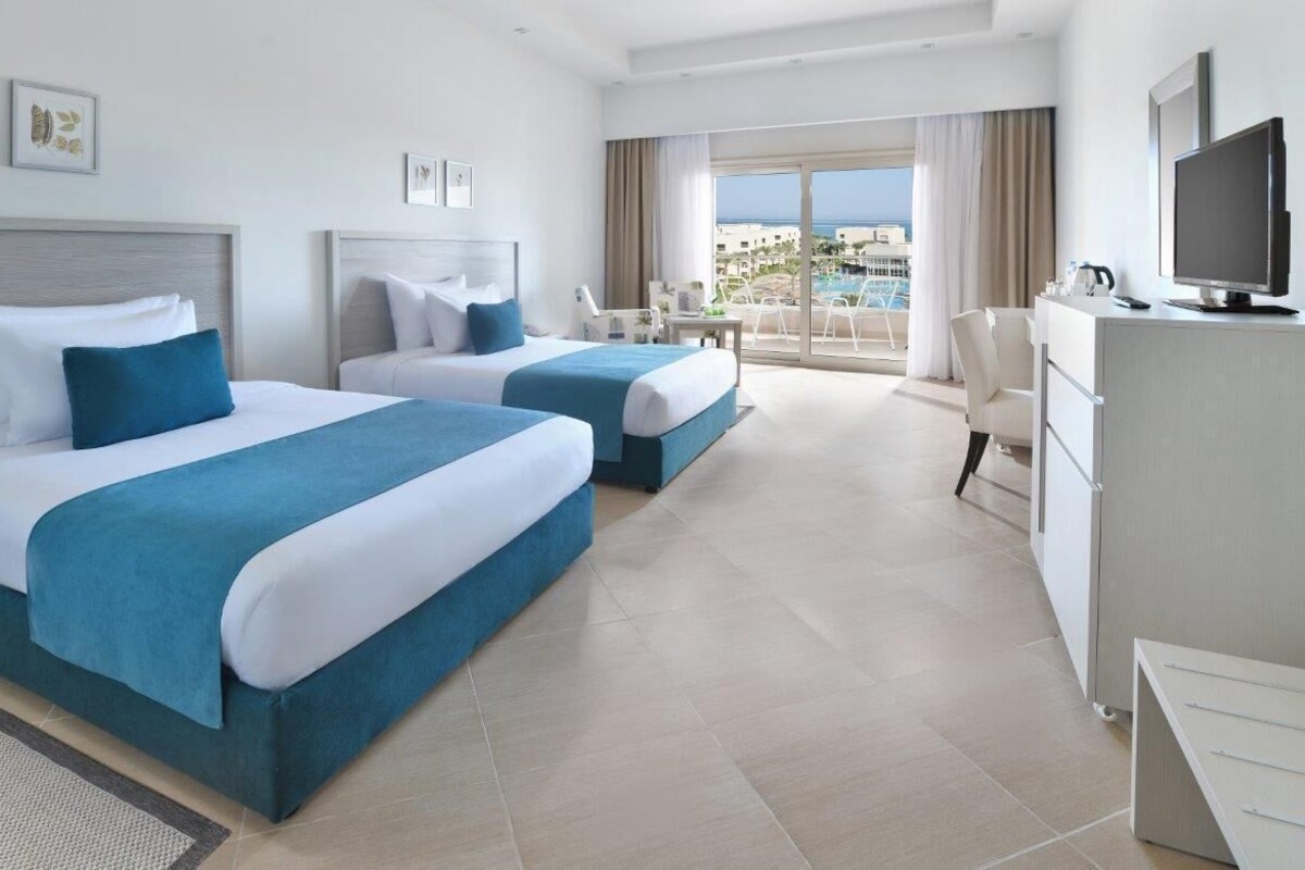 Quarto de hotel com duas camas, uma escrivaninha, televisão e varanda com vista.
