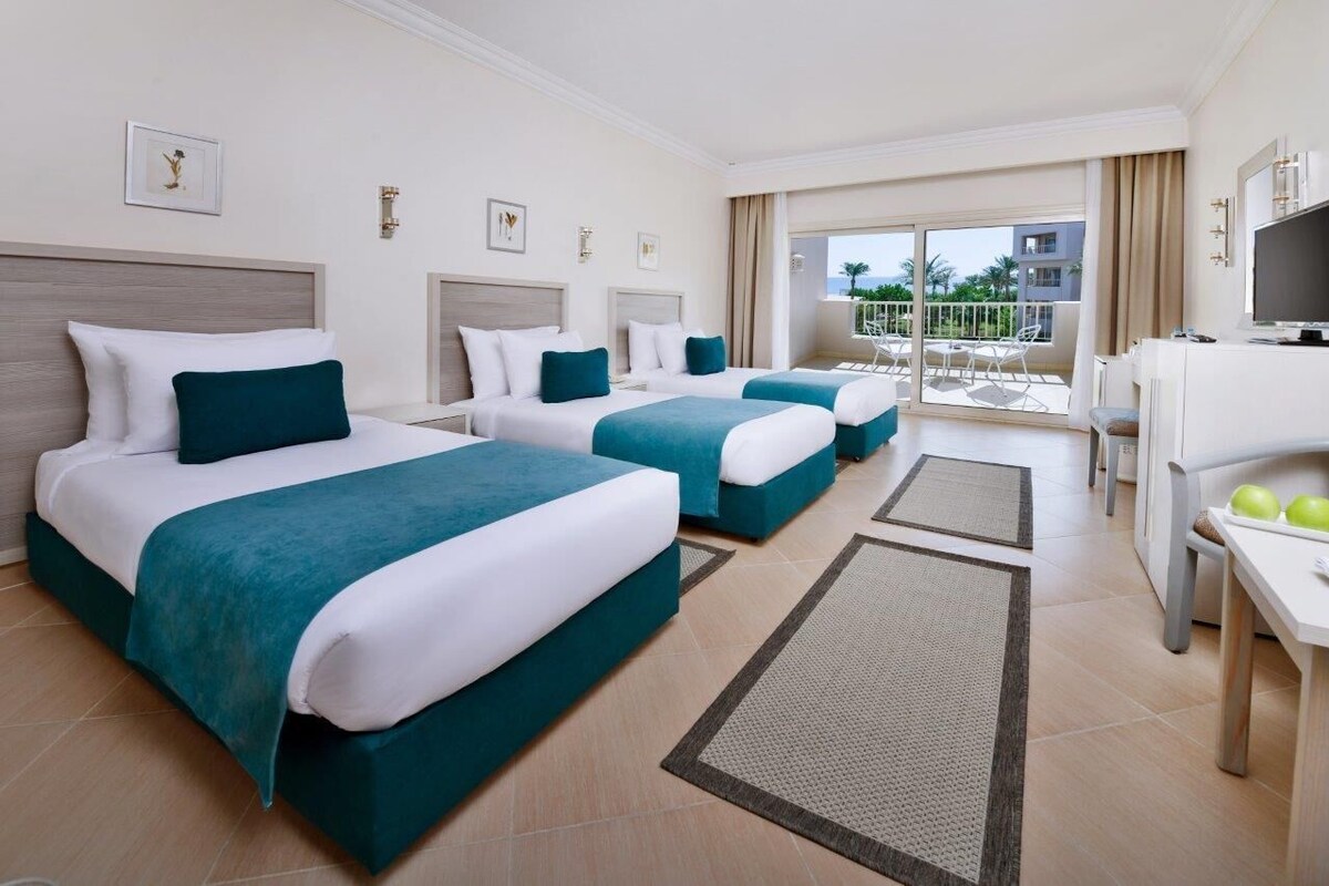 Quarto de hotel com duas camas, televisão, escrivaninha e varanda com vista.