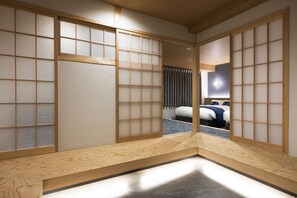 Quarto tradicional japonês com portas deslizantes, uma plataforma de madeira e uma cama com cobertor azul.