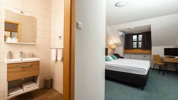 Quarto de hotel com casa de banho, cama, secretária e televisão.