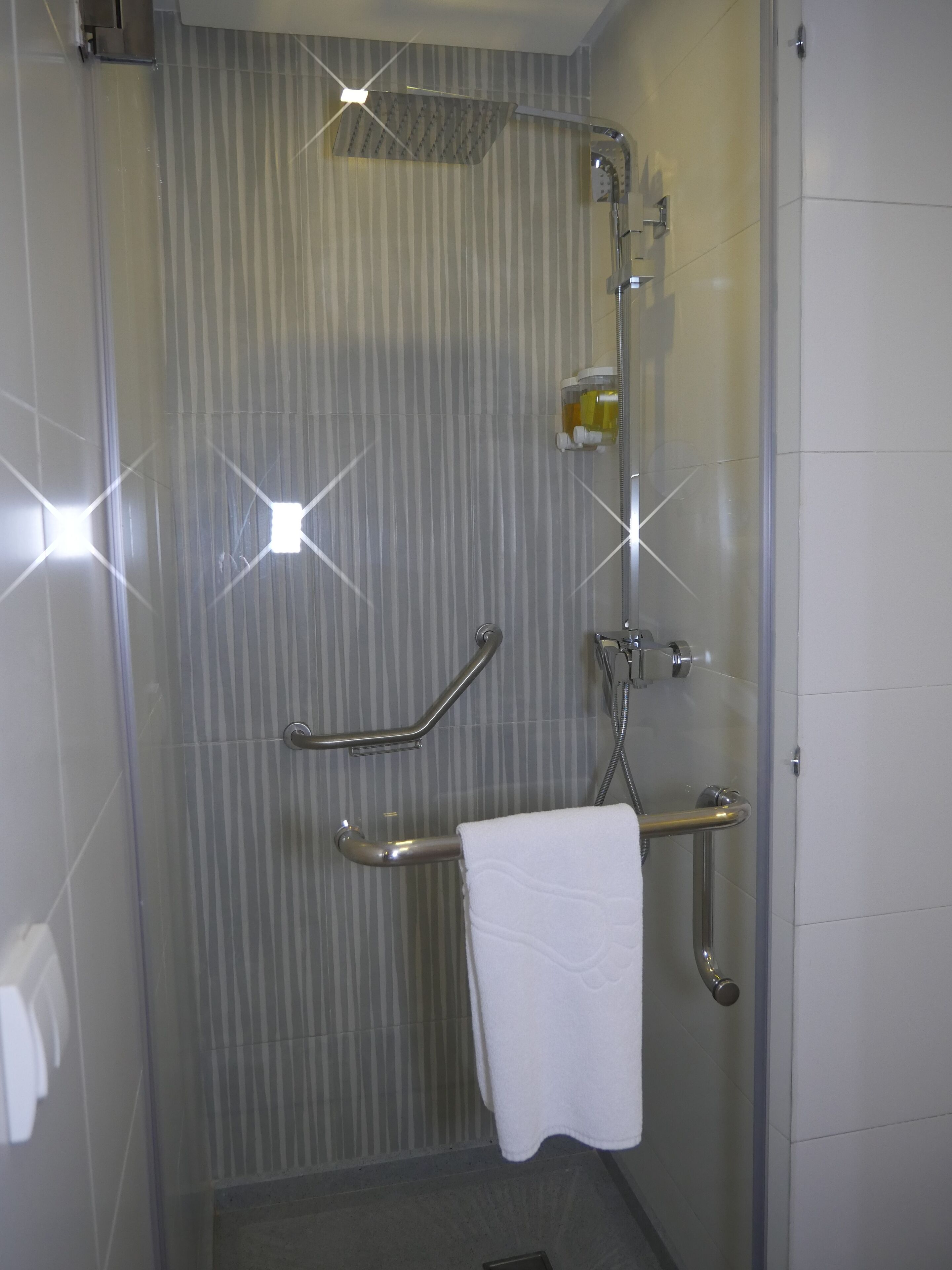 Chuveiro com porta de vidro, barra de apoio e porta-toalhas.