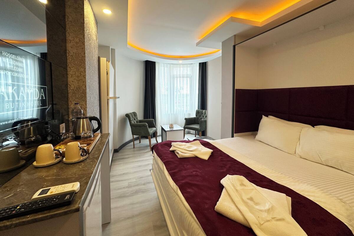 Quarto de hotel com uma cama grande, uma escrivaninha com telefone, televisão e duas cadeiras.