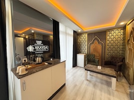 Quarto de hotel moderno com televisão de tela plana, minibar, máquina de café e área de estar com duas cadeiras.
