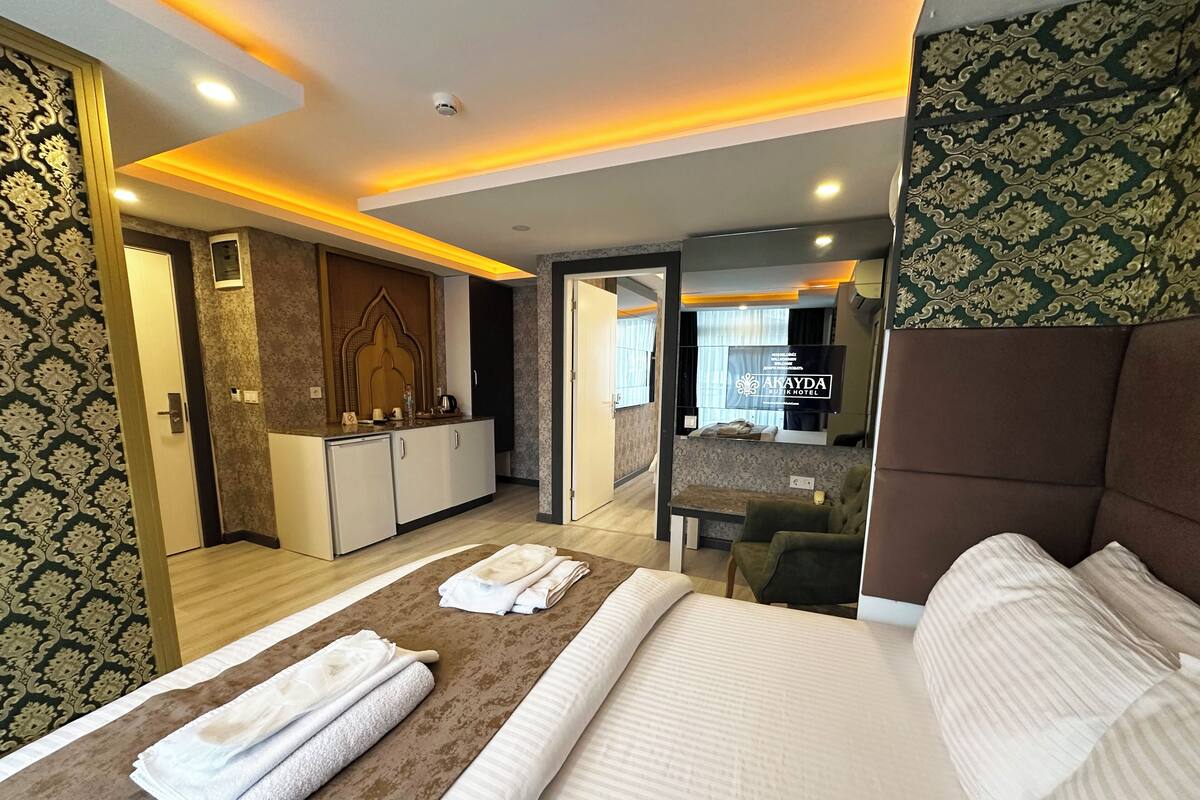 Quarto de hotel com cama, uma pequena escrivaninha, espelho e banheiro visível através de uma porta aberta.