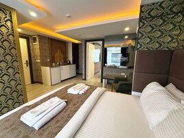 Quarto de hotel com cama, uma pequena escrivaninha, espelho e banheiro visível através de uma porta aberta.