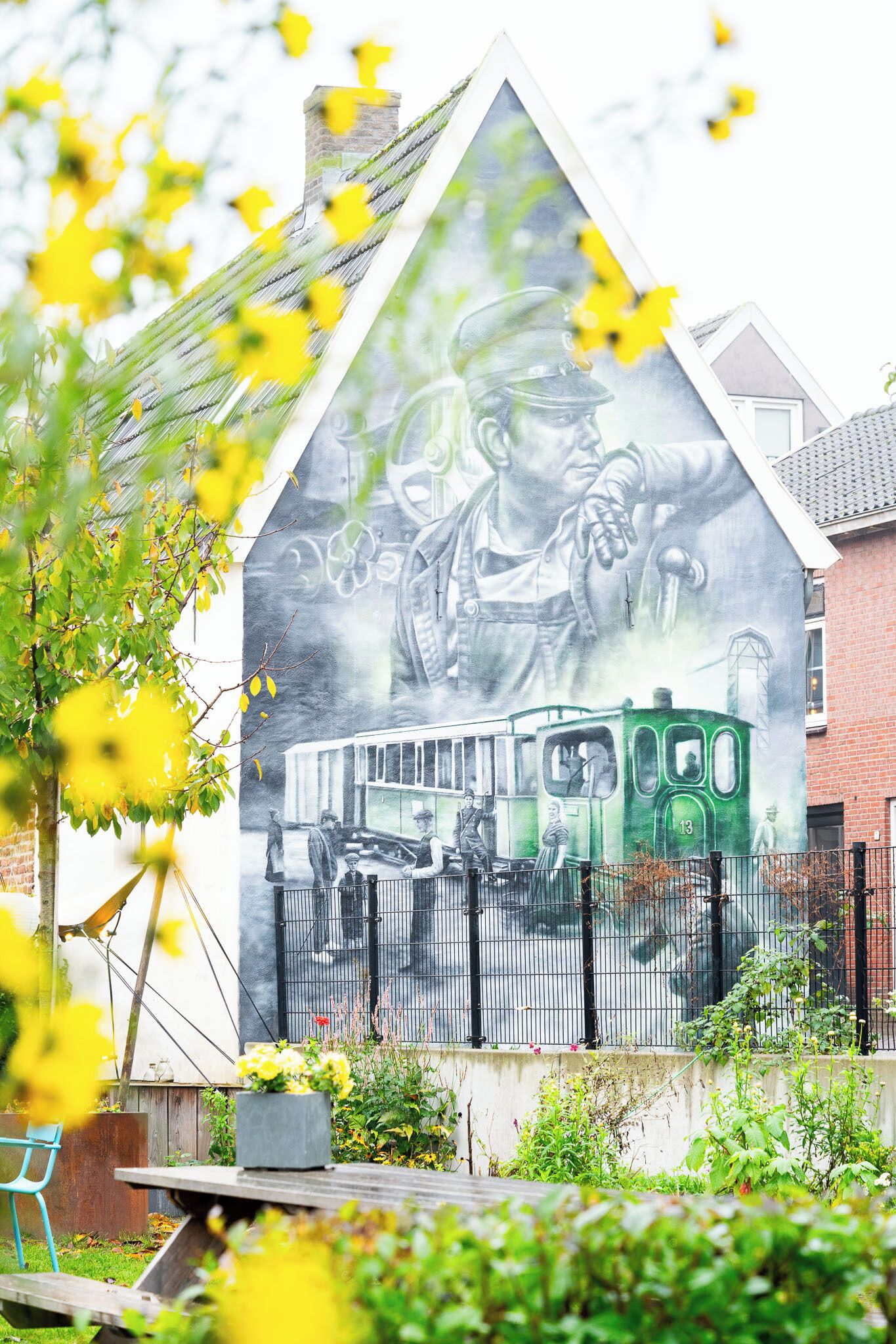 Um mural retrata um elétrico verde com pessoas, um edifício e uma cerca.