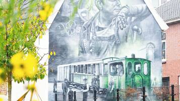 Um mural retrata um elétrico verde com pessoas, um edifício e uma cerca.