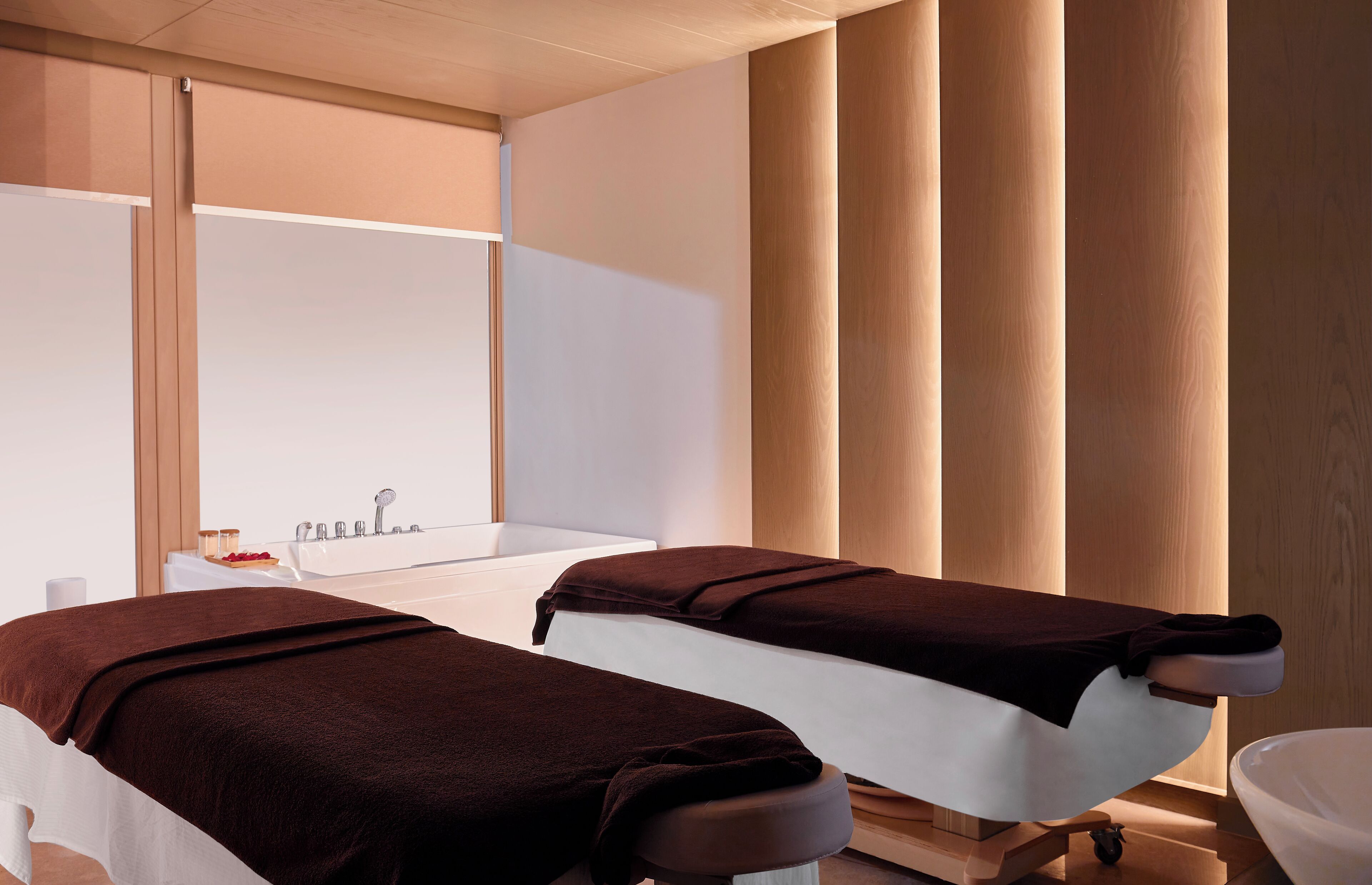 Uma sala de spa moderna com duas macas de massagem, um espelho grande e uma banheira.