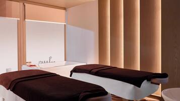 Uma sala de spa moderna com duas macas de massagem, um espelho grande e uma banheira.