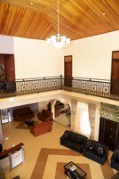 Uma sala de estar ampla com teto alto, uma varanda com guarda-corpo e um lustre.