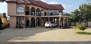 Um edifício de dois andares com área de estacionamento coberta, um carro e um pequeno jardim.