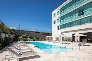 Um hotel moderno com piscina, área de estar externa e um edifício com grandes janelas.