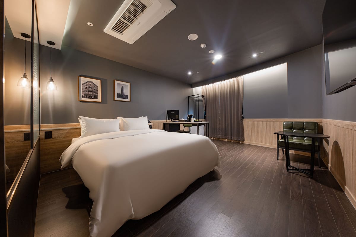 Quarto de hotel moderno com uma cama grande, uma escrivaninha, uma cadeira e um espelho.