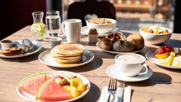 Uma mesa de café da manhã com diversos pratos, incluindo panquecas, croissants e frutas.