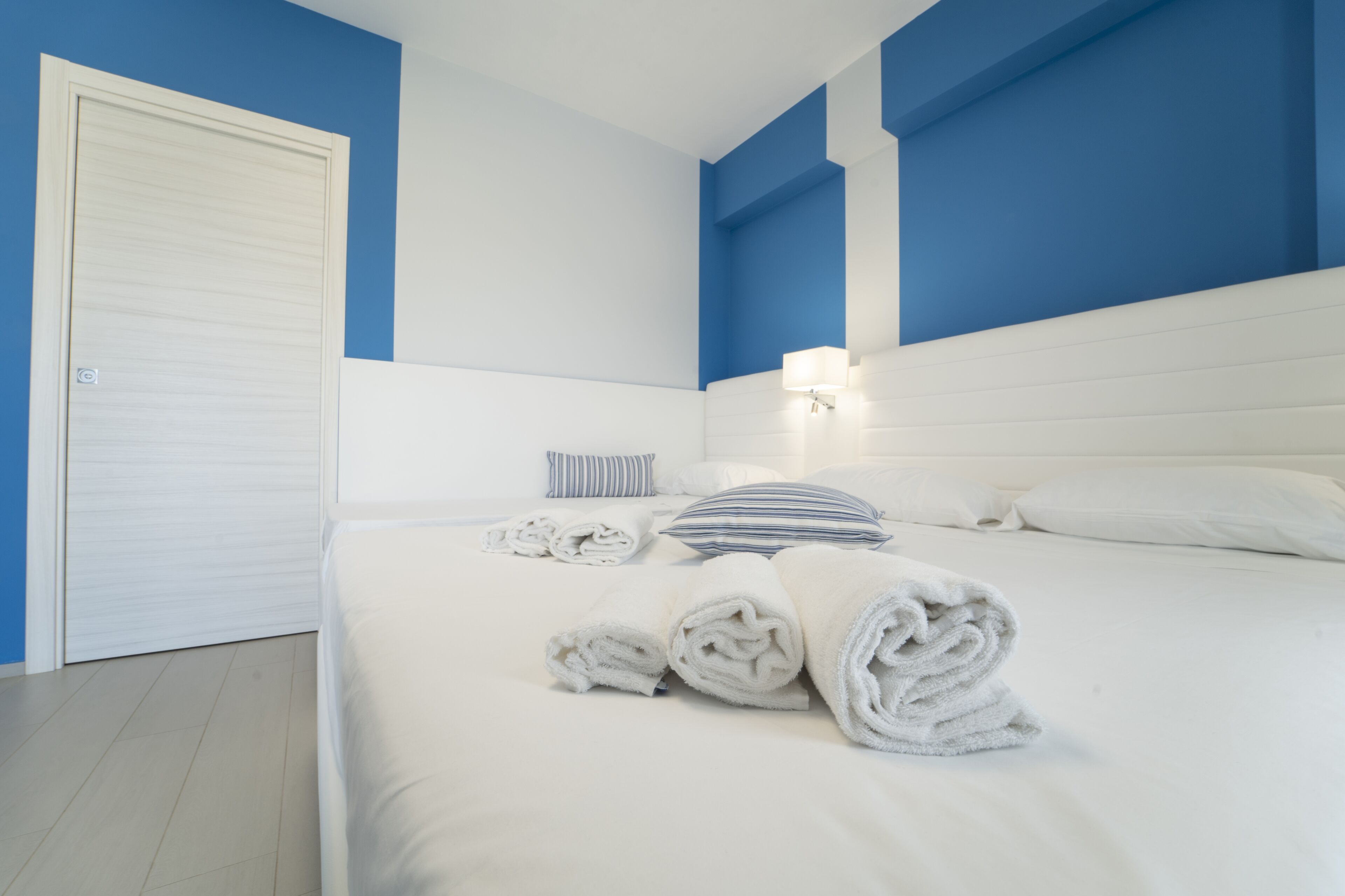 Quarto de hotel com cama, toalhas brancas, almofada listrada e cabeceira branca.