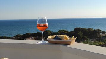 Varanda com um copo de vinho tinto e uma tigela de petiscos, com vista para o mar.