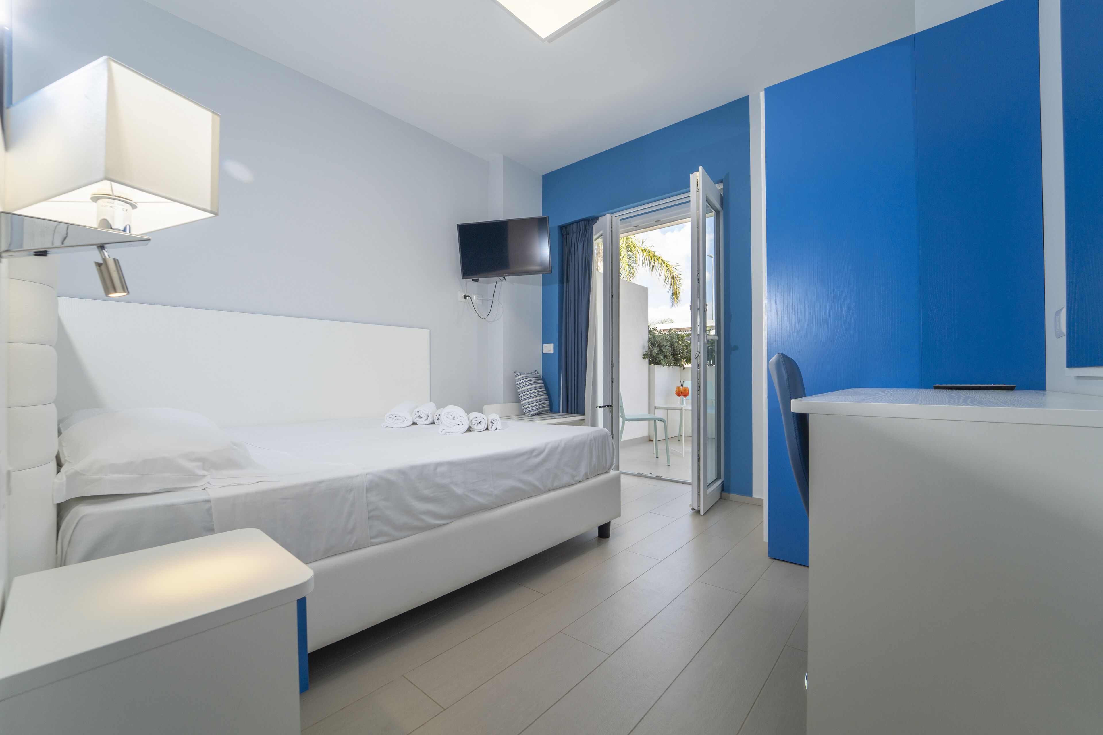 Quarto de hotel moderno com cama, mesa de cabeceira, televisão e vista para o exterior.