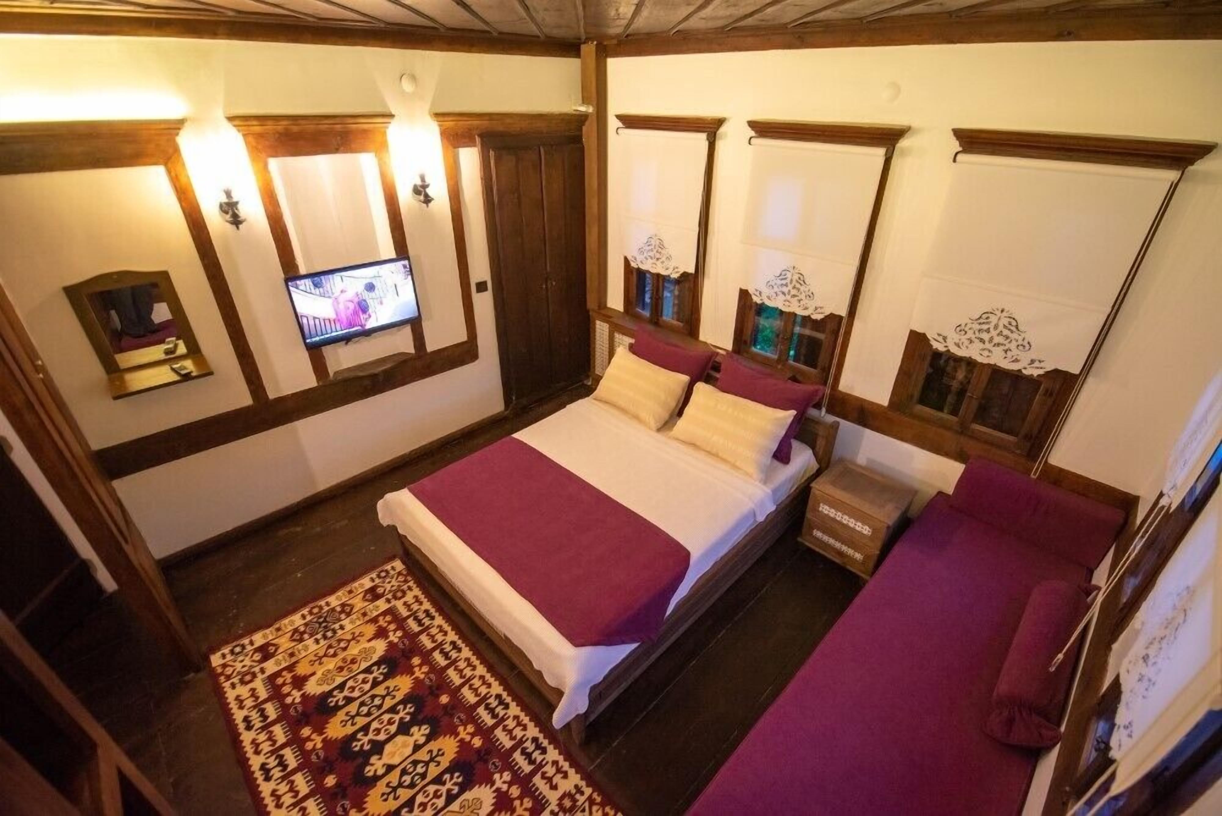 Um quarto com uma cama, uma televisão, um guarda-roupa de madeira e um tapete estampado.
