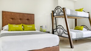 Quarto de hotel com uma cama de solteiro e uma cama beliche, ambos com almofadas verdes com a inscrição "Ayenda Hotels".