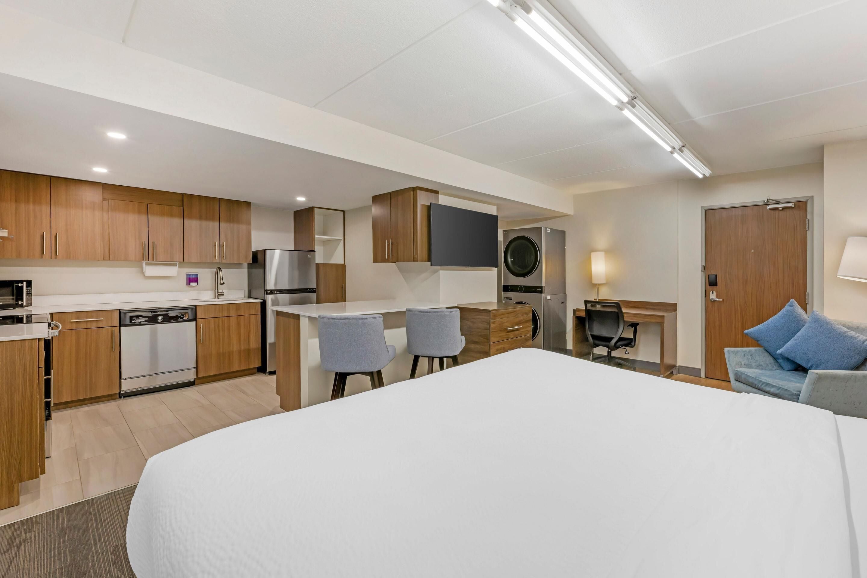 Quarto de hotel moderno com uma cama grande, cozinha compacta, área de refeições e um pequeno escritório.