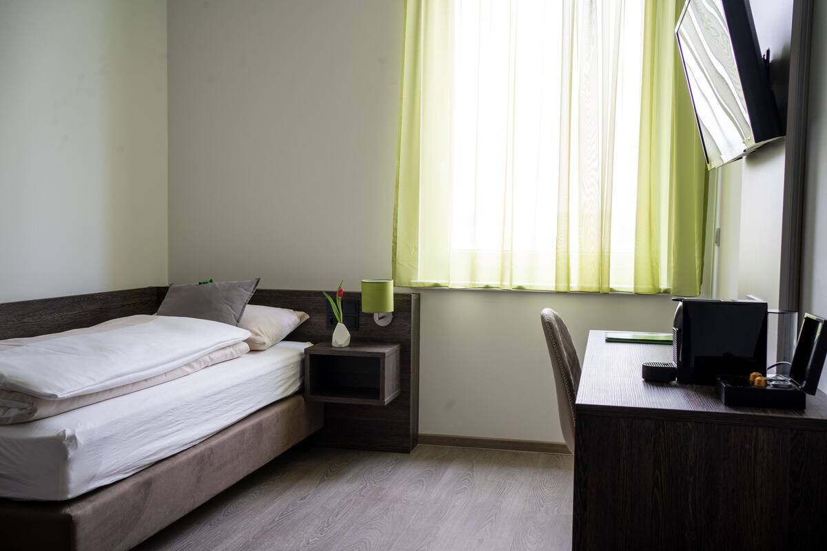 Quarto com cama, mesa de cabeceira, abajur e escrivaninha com computador.