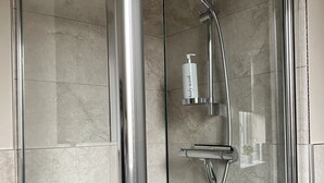 Um chuveiro com paredes de vidro, uma torneira de metal cromado e um dispensador de sabonete numa prateleira.