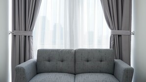 Uma poltrona moderna num quarto com cortinas leves e vista para a cidade.