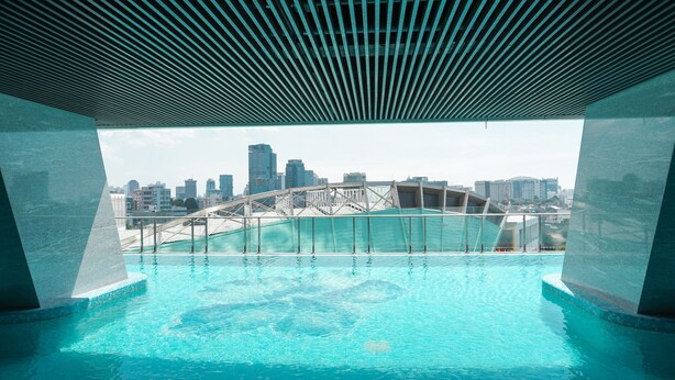 Uma piscina interior moderna com vista para o horizonte urbano, destacando uma estrutura de ponte singular ao fundo.