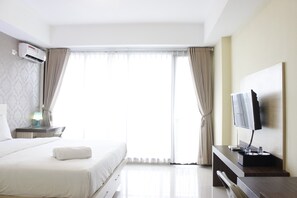 Quarto de hotel com cama, escrivaninha, televisão e janela com cortinas.