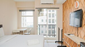 Quarto de hotel com cama, escrivaninha, cadeira, televisão e varanda com vista para edifícios.