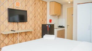 Quarto de hotel com cama, televisão de tela plana na parede, frigorífico, pequena cozinha e guarda-roupa.
