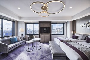 Quarto de hotel moderno com vista para a cidade, um sofá, uma cama, uma mesinha e uma televisão.