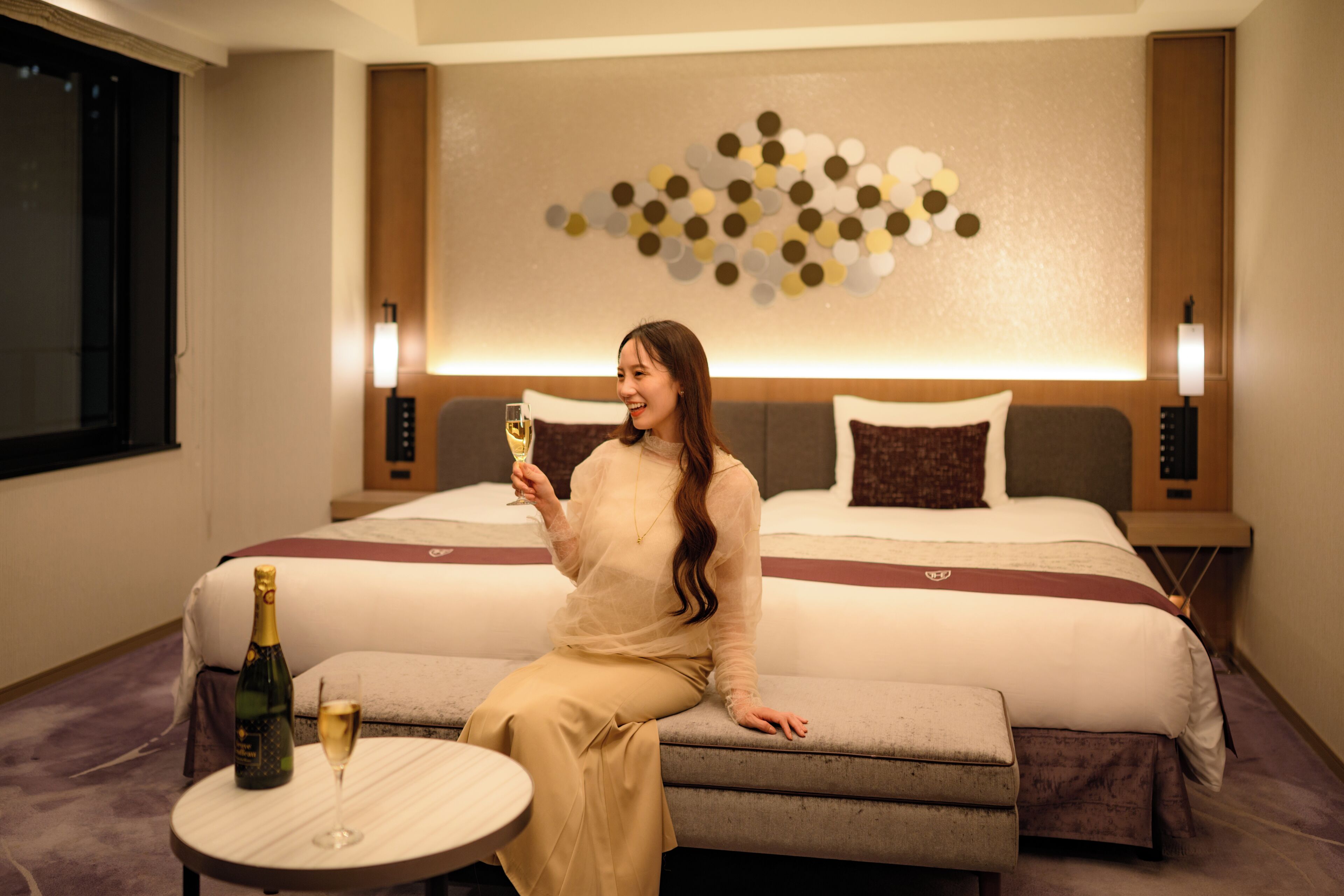Quarto de hotel com uma cama, uma mesa de cabeceira com uma garrafa e um copo, e um objeto decorativo na parede.