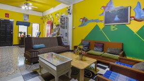 Uma sala de estar vibrante, com um sofá, uma mesa de centro e uma parede com murais coloridos.
