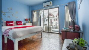 Quarto com cama, escrivaninha, televisão e varanda com vista para edifícios.