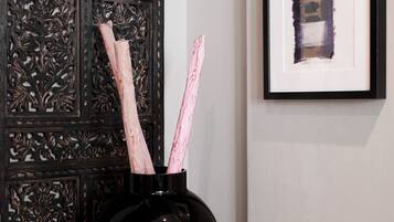 Um vaso preto com gravetos rosa e brancos listrados sobre uma mesa preta, em frente a uma parede com um painel ornamentado e uma pintura abstrata emoldurada.