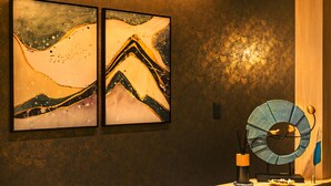 Duas pinturas abstratas numa parede texturizada, uma peça de metal decorativa com um pássaro, e uma prateleira de madeira com uma tigela e pauzinhos.