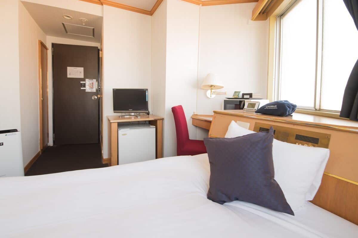 Quarto de hotel com cama, escrivaninha, cadeira e janela.