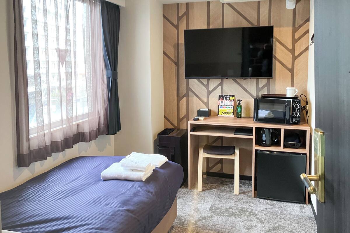 Quarto de hotel com cama, escrivaninha, televisão de tela plana, micro-ondas e pequeno frigorífico.