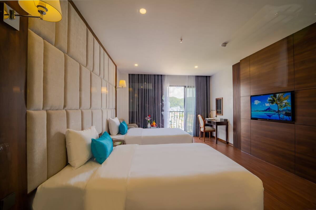 Quarto de hotel moderno com duas camas, televisão, varanda e uma escrivaninha.