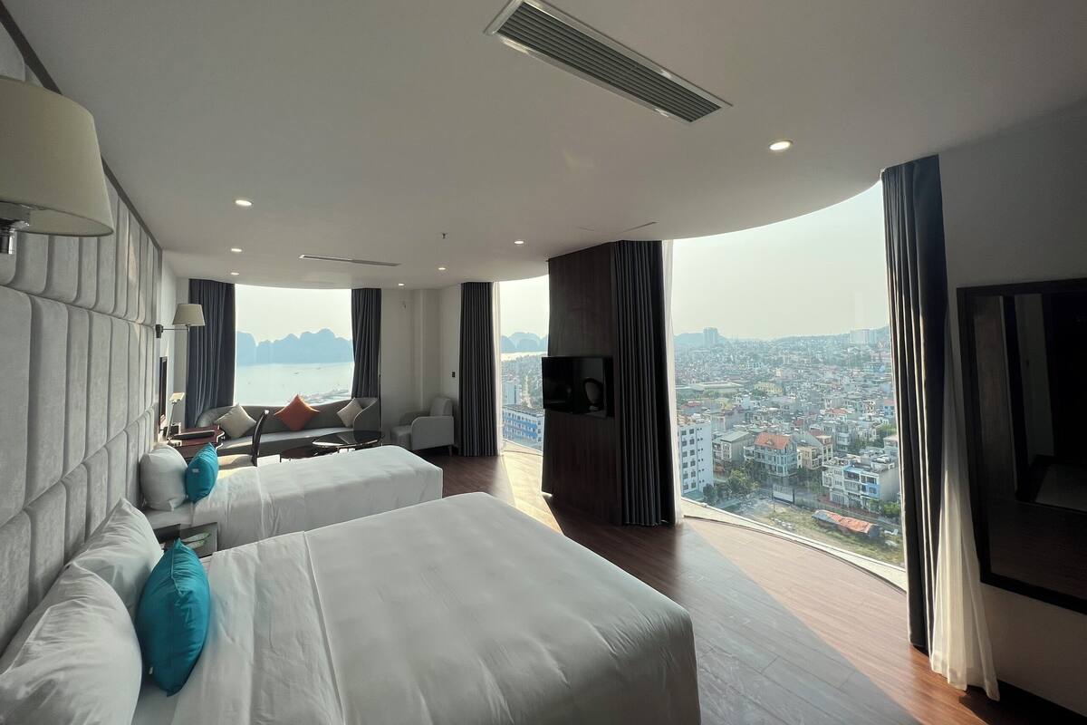 Quarto de hotel moderno com uma cama grande, um sofá, uma TV e vista para a cidade.