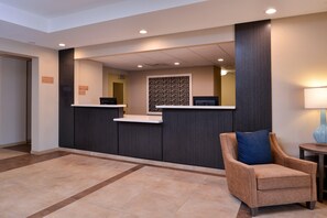 Uma área de recepção com balcão, uma cadeira com almofada e um painel decorativo na parede.