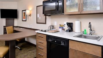 Cozinha compacta de hotel equipada com micro-ondas, cafeteira e máquina de lavar louça.