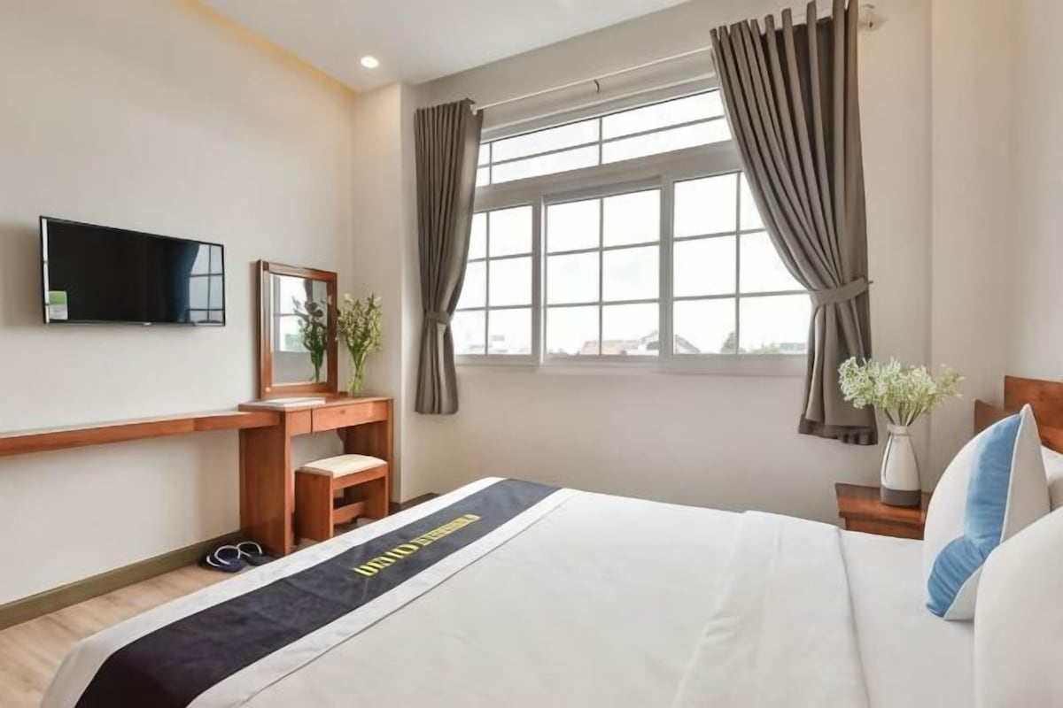 Quarto de hotel com cama, escrivaninha, televisão, janela com cortinas e vista para a cidade.