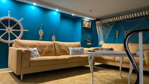 Uma sala de estar com dois sofás, uma mesa de centro e decoração temática náutica, incluindo um leme de navio e redes.