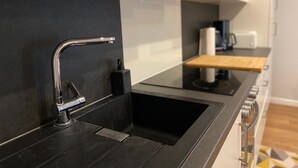 Uma cozinha moderna com uma pia de aço inoxidável, bancada preta e armários brancos.
